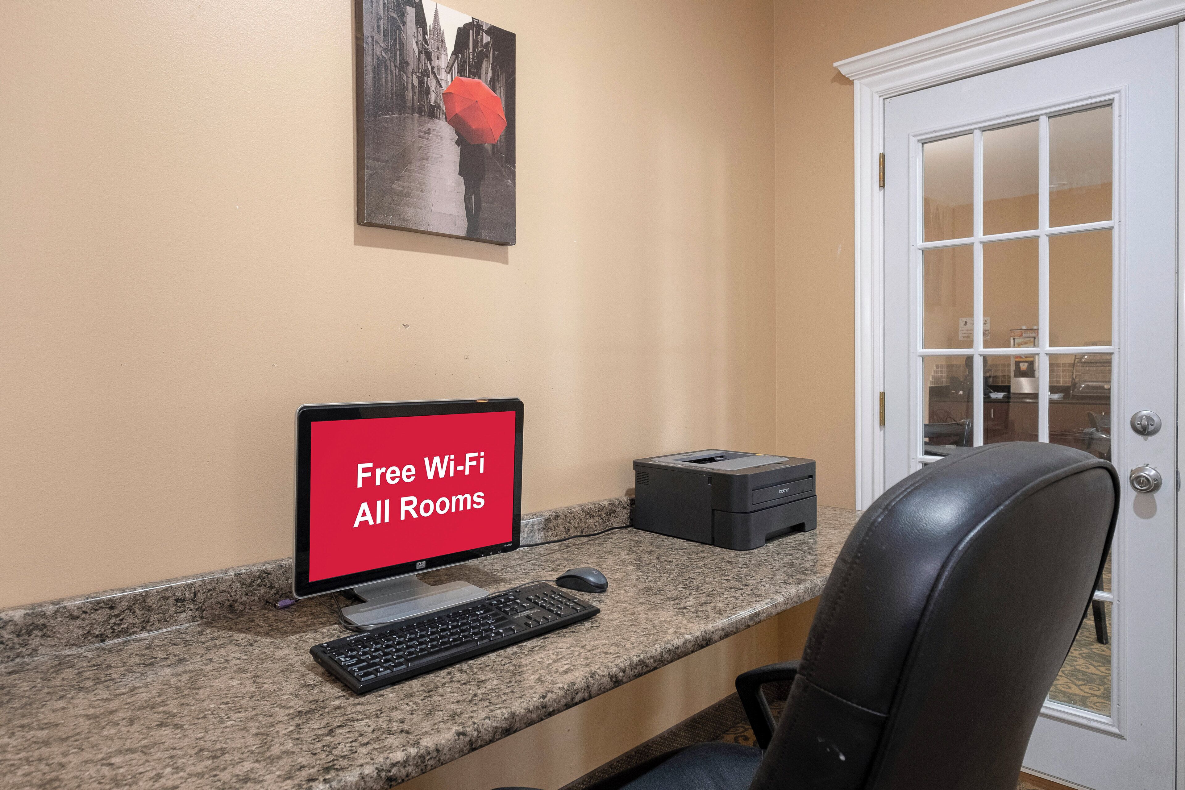 Quarto de hotel com uma escrivaninha, computador, impressora e uma cadeira.