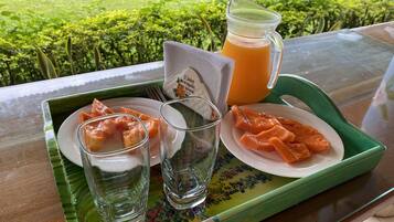 Uma bandeja com pratos de comida, copos e um jarro de suco sobre uma mesa com vista para um jardim verde.