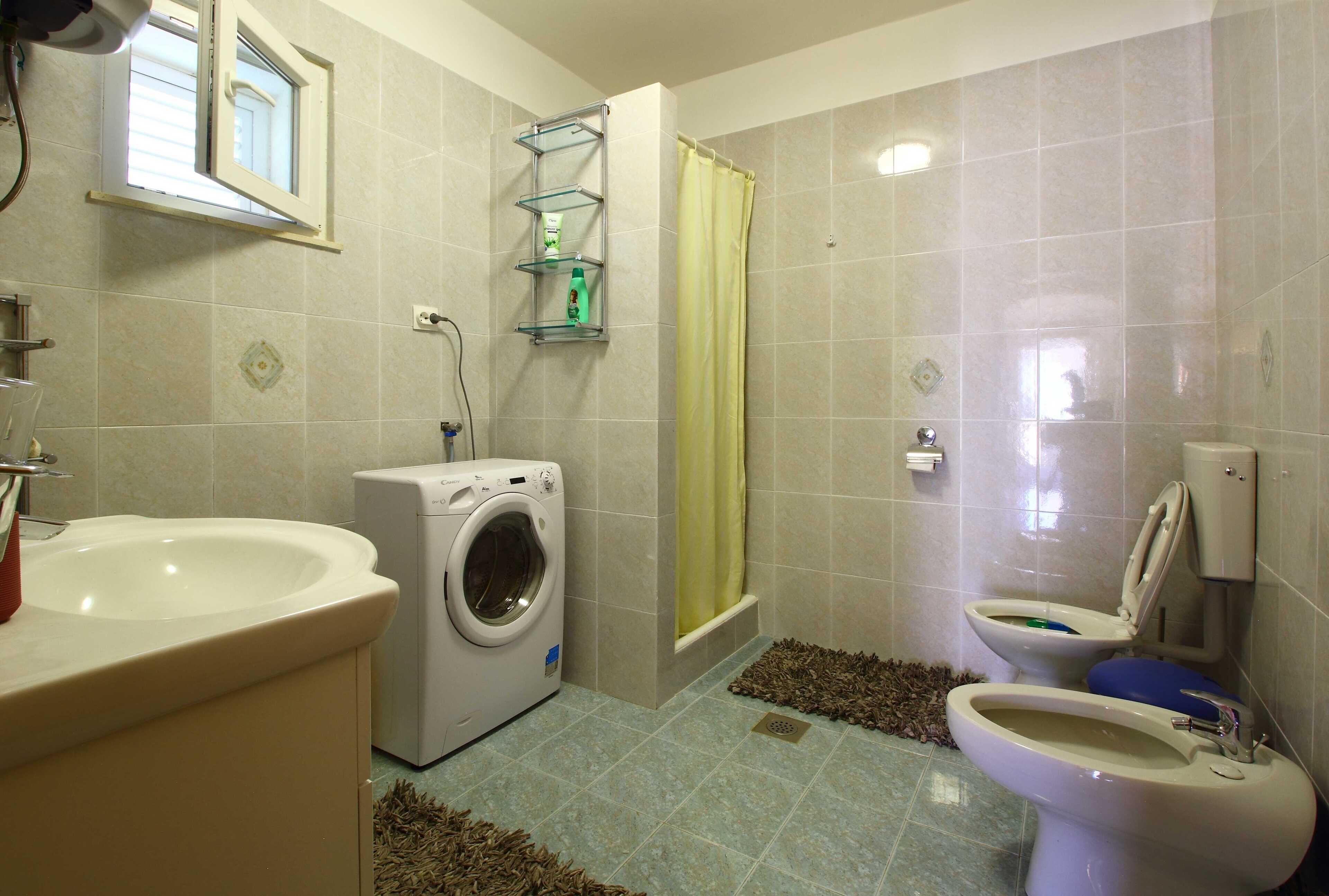Casa de banho compacta com lavatório, máquina de lavar roupa, duas sanitas e chuveiro.