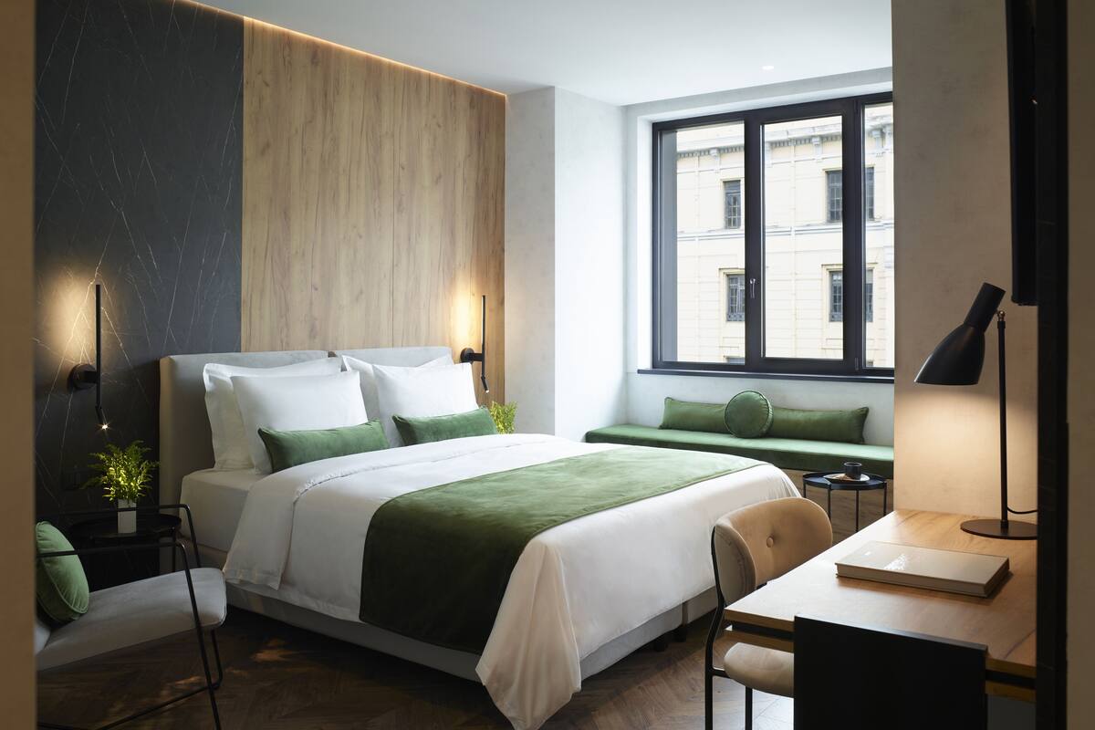 Quarto de hotel moderno com uma cama grande, uma escrivaninha e uma janela vista para a cidade.