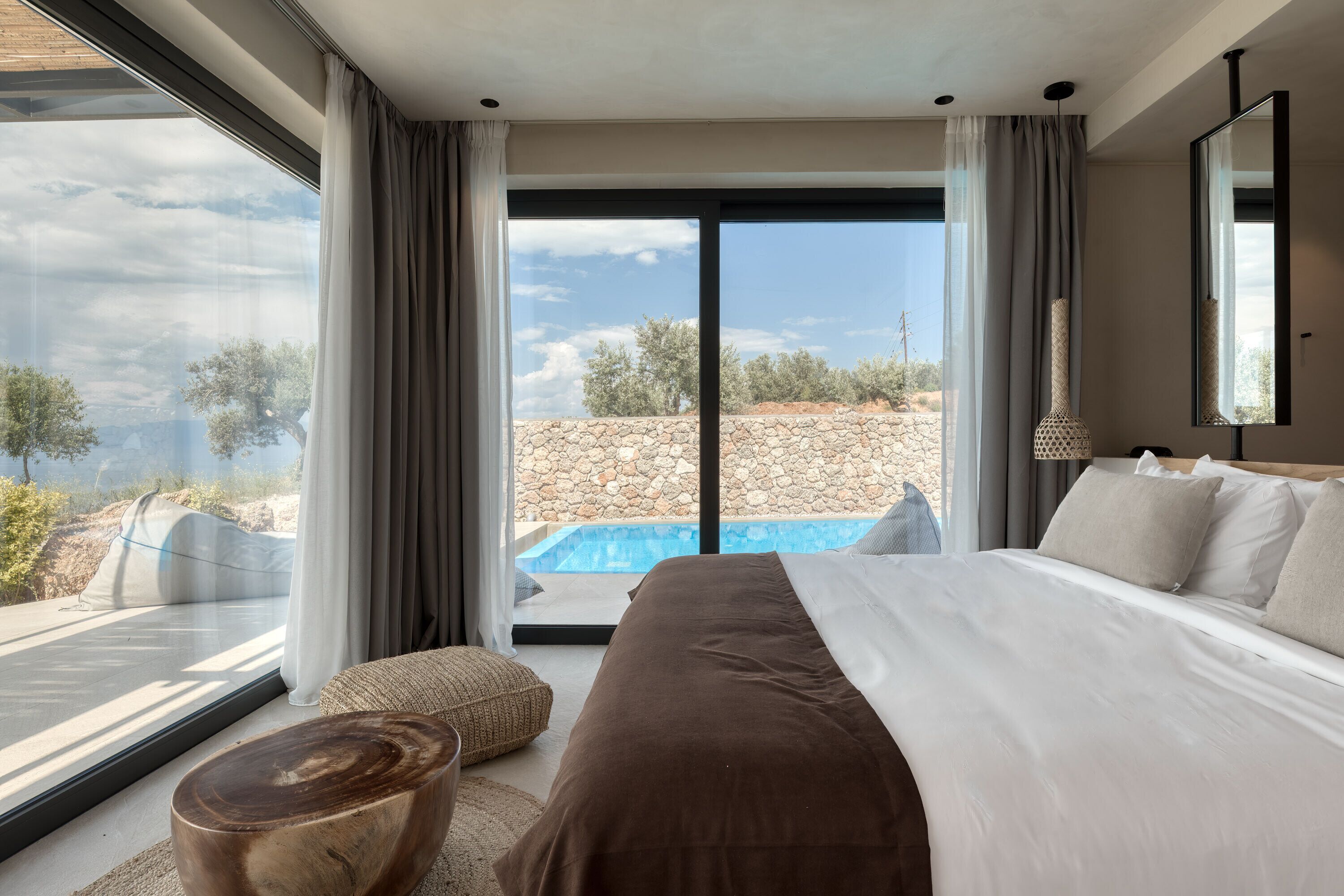 Quarto moderno com uma cama grande, vista para uma piscina e parede de pedra externa.