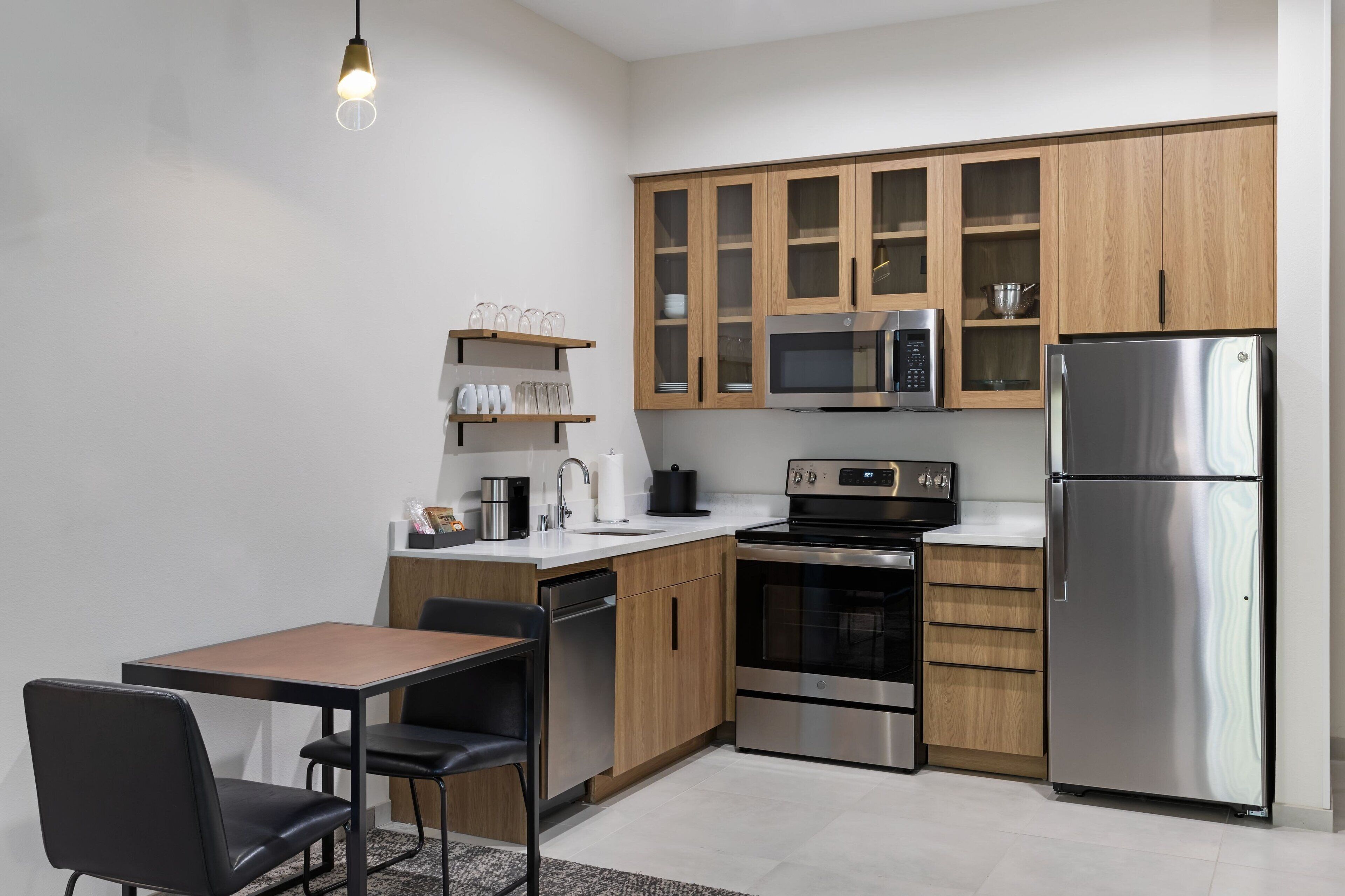 Uma cozinha compacta com armários de madeira, eletrodomésticos de aço inoxidável, uma área de jantar com mesa e cadeiras, e um lustre.