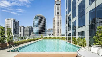Piscina no terraço com deck de madeira, rodeada por edifícios modernos e vegetação.