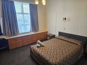 Quarto com cama, penteadeira, escrivaninha e janela com cortinas.