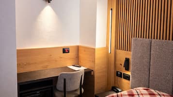 Quarto de hotel com cama, escrivaninha, cadeira, luminária na parede, telefone e painel de parede em madeira.