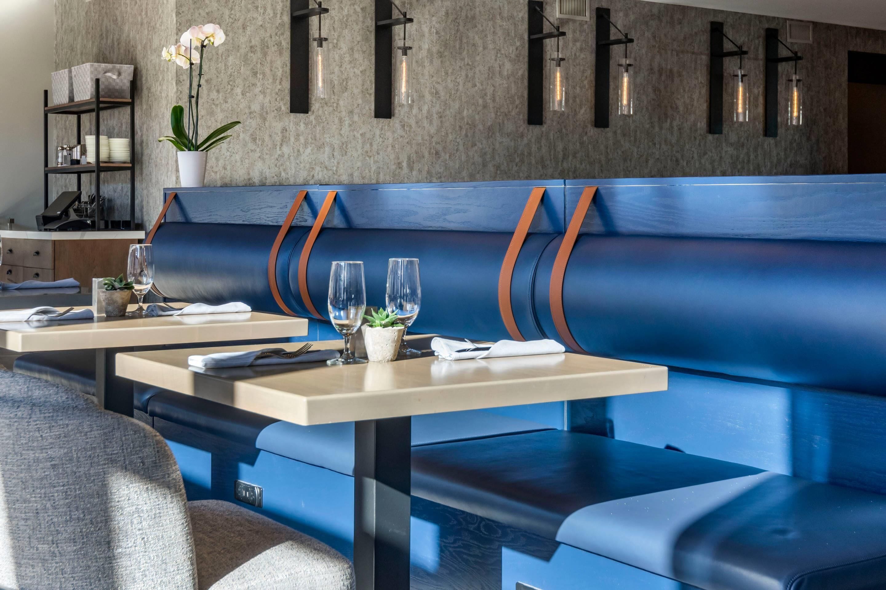 Um restaurante moderno com assentos acolchoados em azul, mesas de madeira e iluminação pendente.