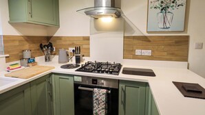 Cozinha moderna com armários verdes, fogão a gás, forno e coifa de aço inoxidável.