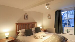 Uma cama bem arrumada com um cobertor xadrez, duas luminárias de cabeceira e uma janela com cortinas.