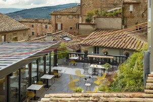 Terraço no telhado com área de estar ao ar livre, estrutura de vidro e vista dos edifícios ao redor.
