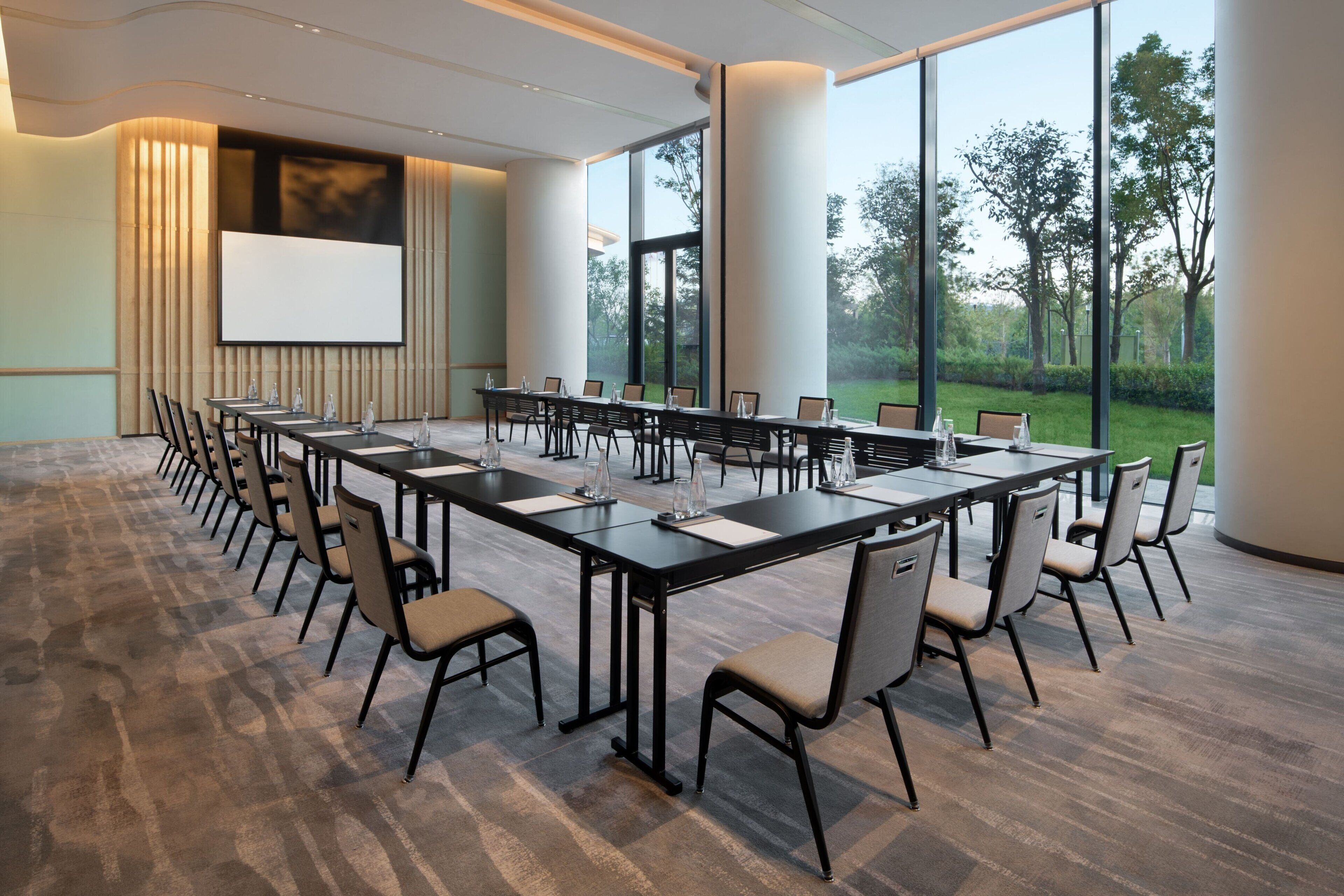 Uma sala de conferências com uma mesa comprida, cadeiras, um projetor e janelas amplas com vista para o exterior.