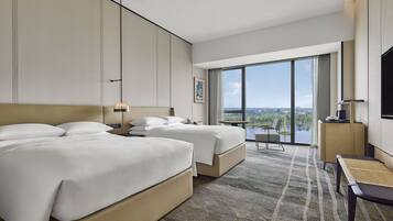 Quarto de hotel com duas camas, uma janela grande com vista, televisão de tela plana e uma mesa pequena.