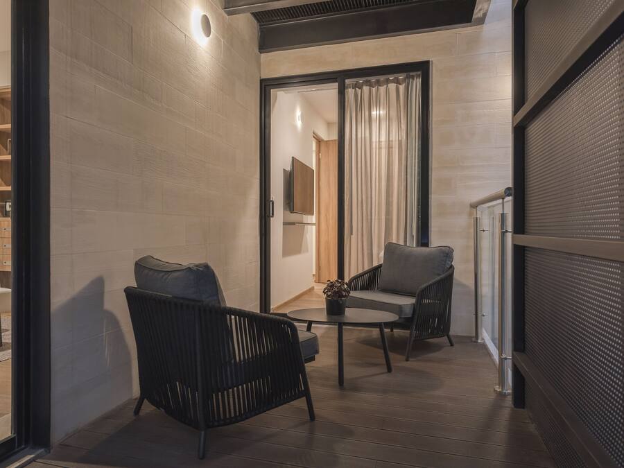 Um interior moderno com sofá, duas cadeiras, uma mesa pequena e uma televisão num quarto com soalho de madeira e paredes.