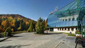 Um hotel com fachada de vidro moderna, área de entrada pavimentada e vista para uma encosta arborizada.