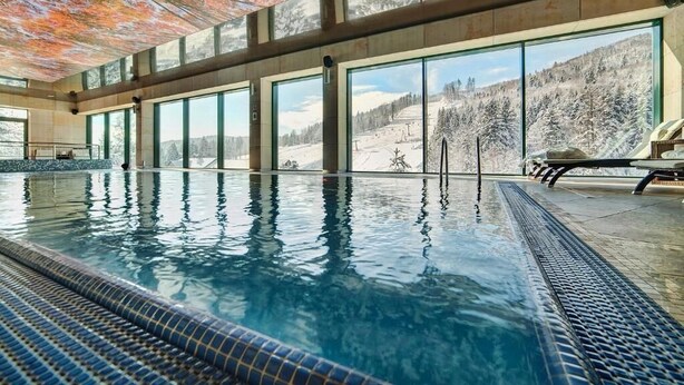 Piscina interior com vista clara para uma paisagem montanhosa coberta de neve através de grandes janelas.