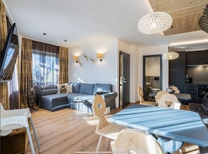 Uma sala de estar moderna com um sofá seccional, uma mesa de jantar com cadeiras e uma cozinha visível através de uma porta aberta.