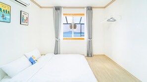 Quarto com cama, janela com cortinas, luminária pendente e quadros nas paredes.