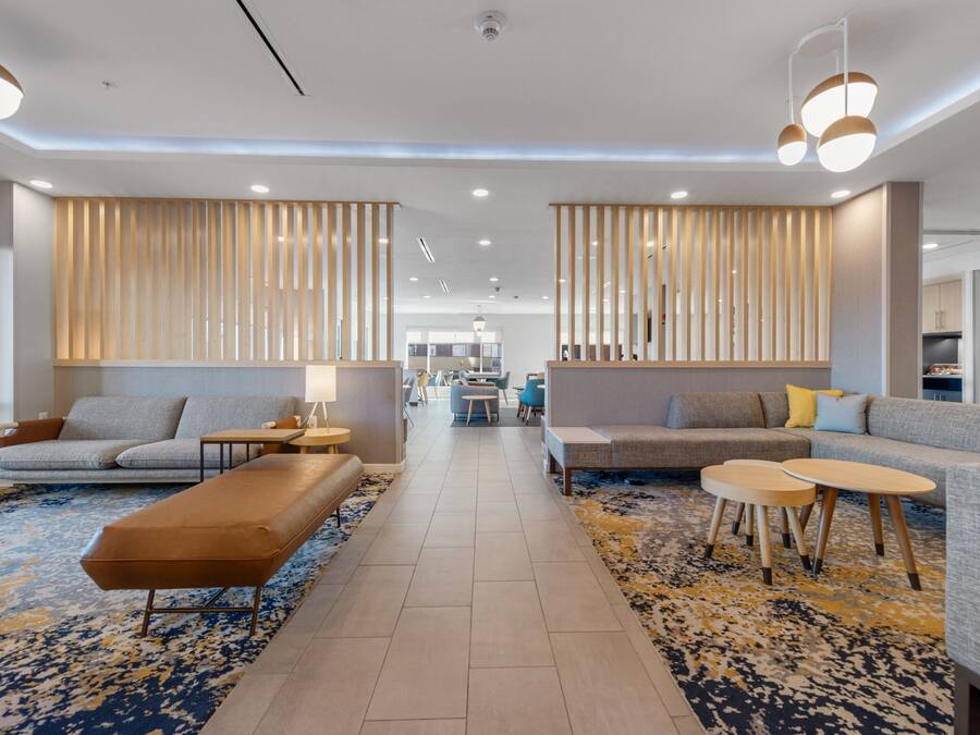 Um saguão moderno de hotel, com área de estar central, balcão de recepção e vista para a sala de jantar.