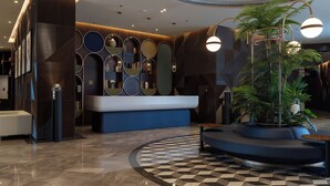 Um lobby moderno com piso xadrez, área de estar central e uma parede com espelhos circulares.