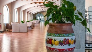 Um hall amplo com teto de madeira alto, um vaso decorativo grande com motivos de frutas e piso de azulejos.
