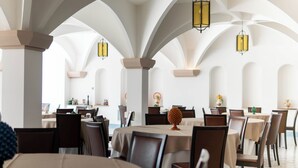 Uma ampla sala de jantar com tetos altos em arco e várias mesas preparadas para refeições.
