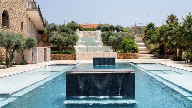 Piscina com cascata, rodeada por edifícios de pedra e vegetação.