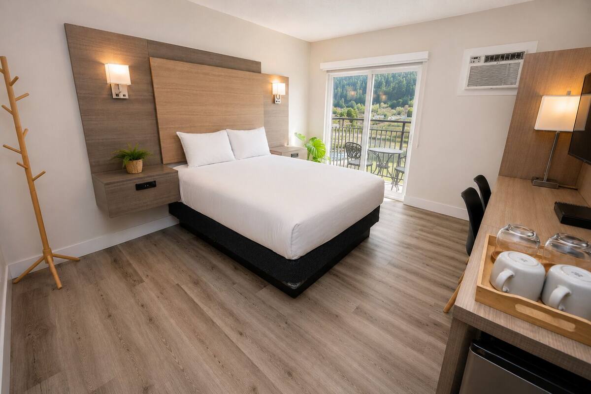 Quarto de hotel moderno com uma cama, mesas de cabeceira, um cabideiro, uma varanda com vista e uma escrivaninha com um jogo de copos.