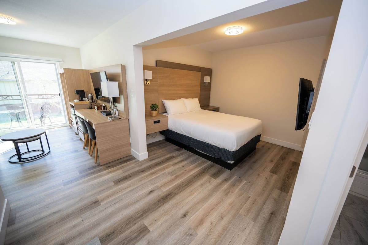 Quarto de hotel moderno com cama, escrivaninha, cadeira e televisão.