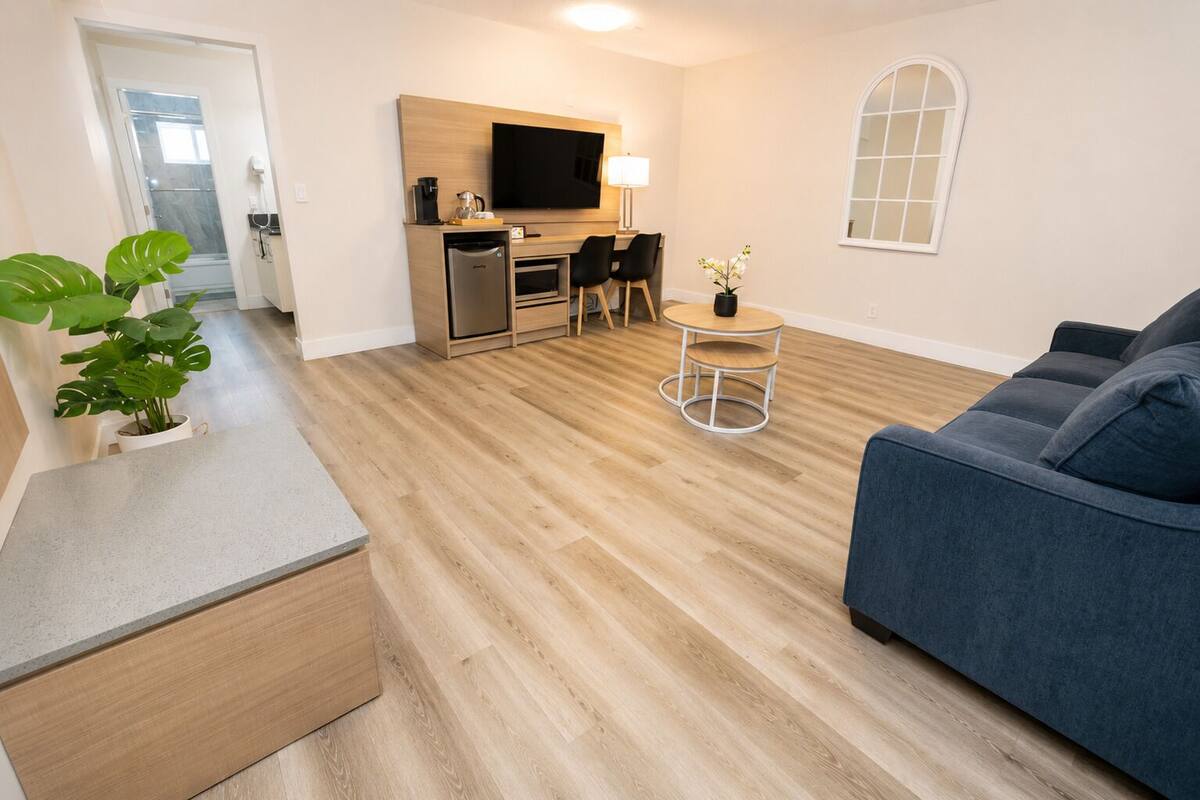 Uma sala de estar moderna com sofá, mesa de centro e área de cozinha com televisão e eletrodomésticos.