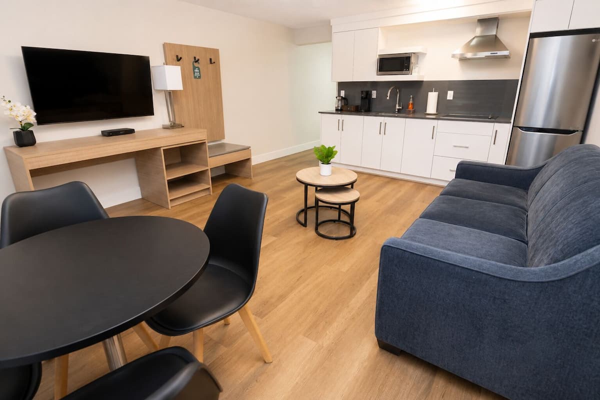 Uma sala de estar moderna com televisão, sofá, mesa de jantar, cadeiras e área de cozinha com eletrodomésticos.