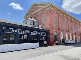 Um edifício de tijolos com uma placa que diz "HOLLINS MARKET" e um carro branco estacionado na frente.