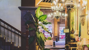 Um amplo saguão com um grande candelabro, uma escadaria com corrimãos ornamentados e uma placa indicando um hotel.