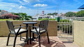 Um pátio com duas cadeiras e uma mesa, com vista para uma marina com barcos e um farol.