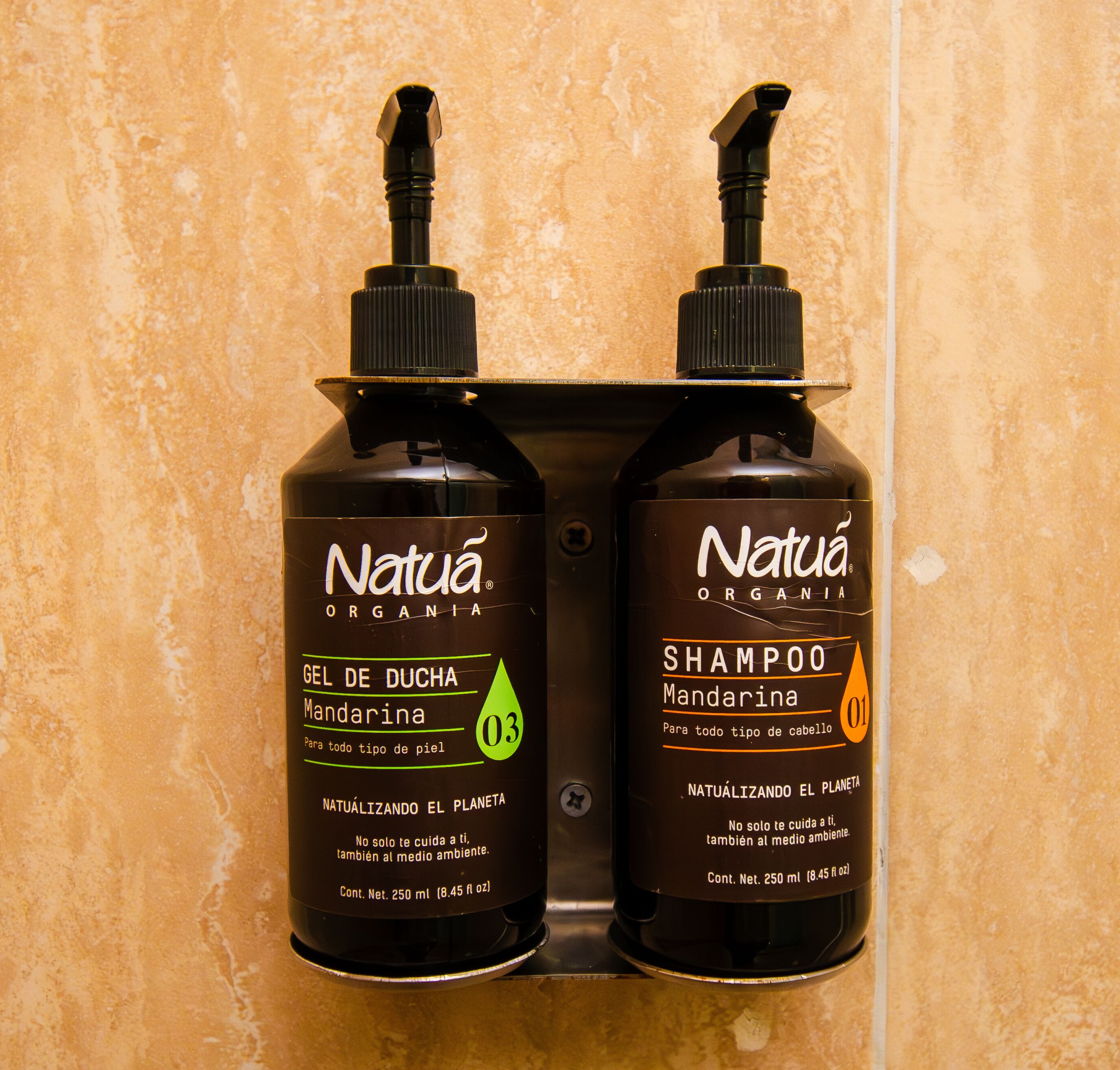 Duas embalagens de shampoo e condicionador Natuà Organía numa parede de banheiro.