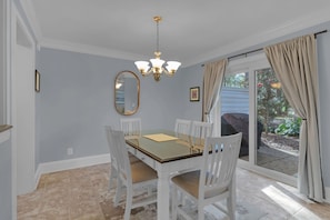 Uma sala de jantar com mesa, cadeiras, um lustre e uma porta de vidro deslizante para um jardim.