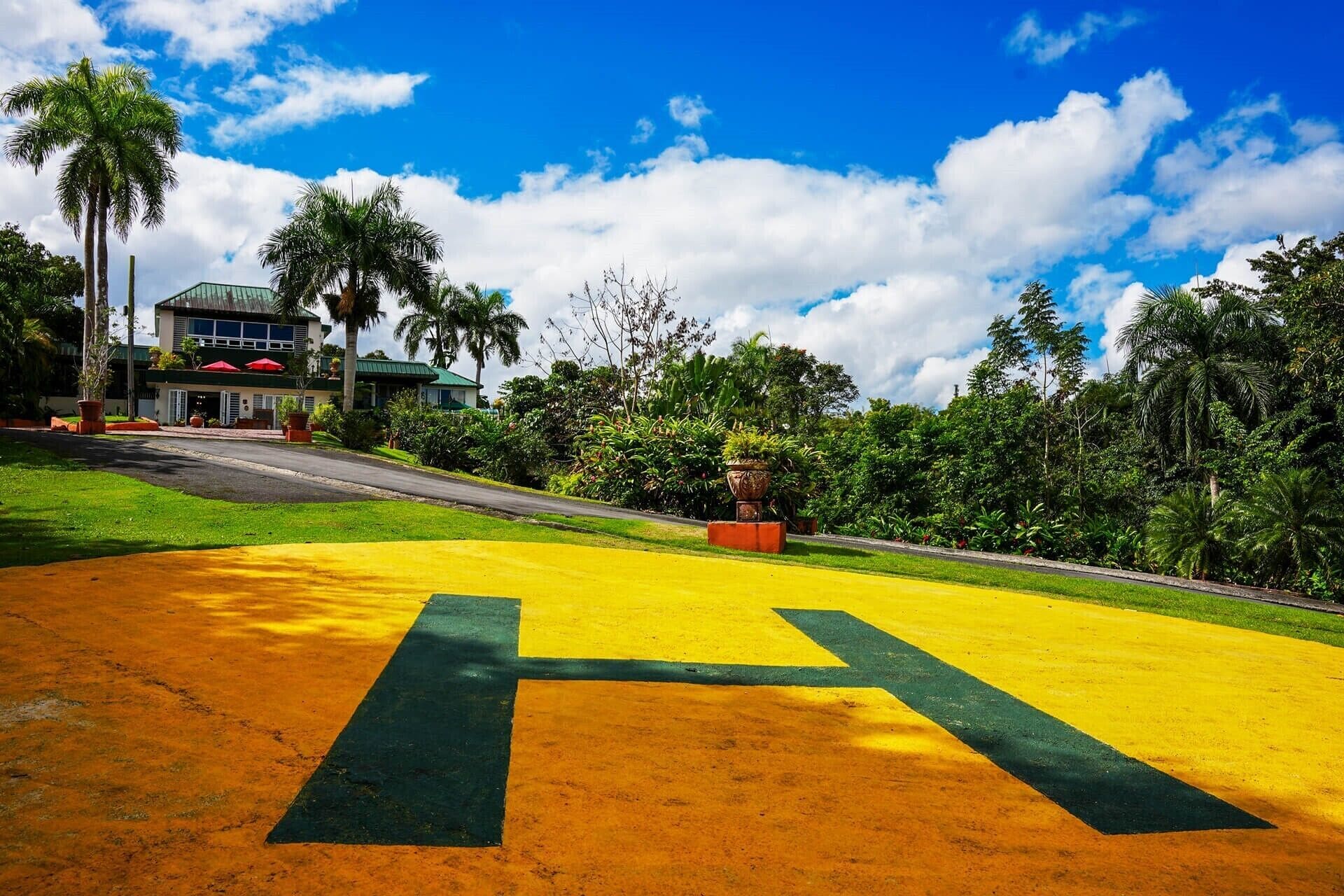 Entrada de hotel com um amplo caminho em formato de H, vegetação exuberante e céu azul límpido.