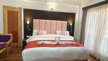 Quarto com uma cama grande, um ventilador de teto, uma porta de madeira, uma mesa pequena e uma cadeira.
