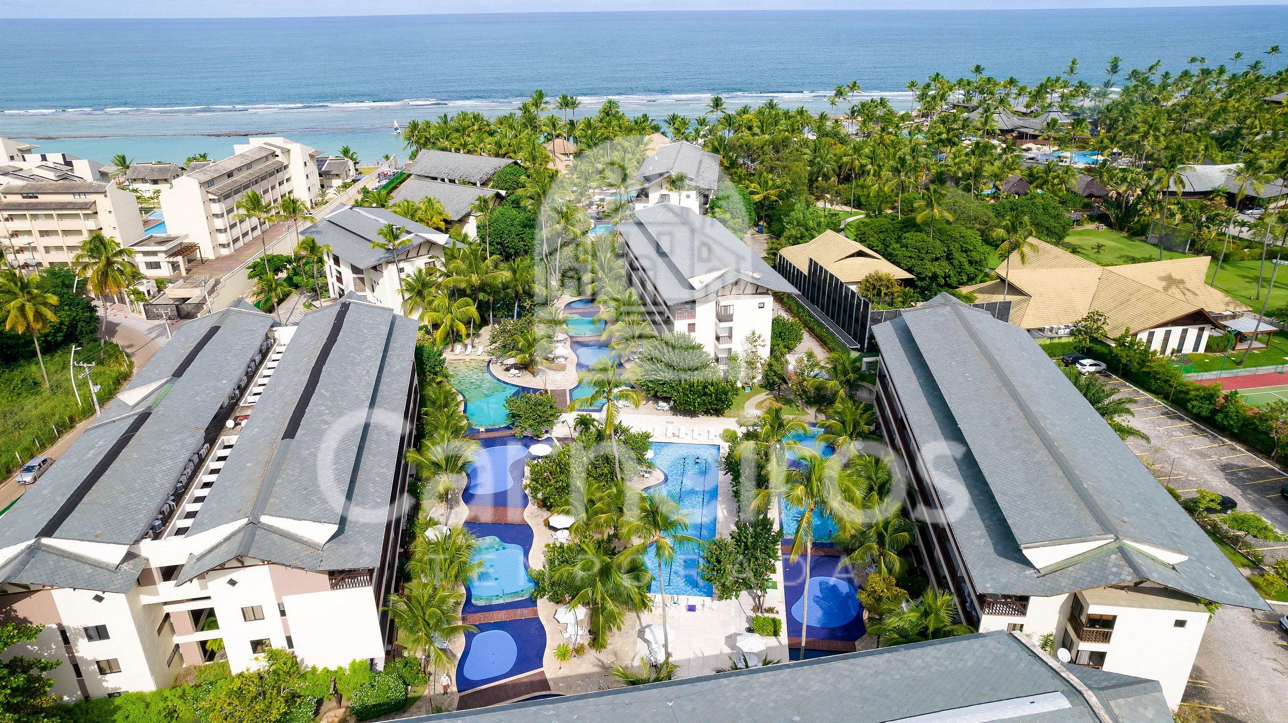 Resort com várias piscinas, vista para a praia e palmeiras.
