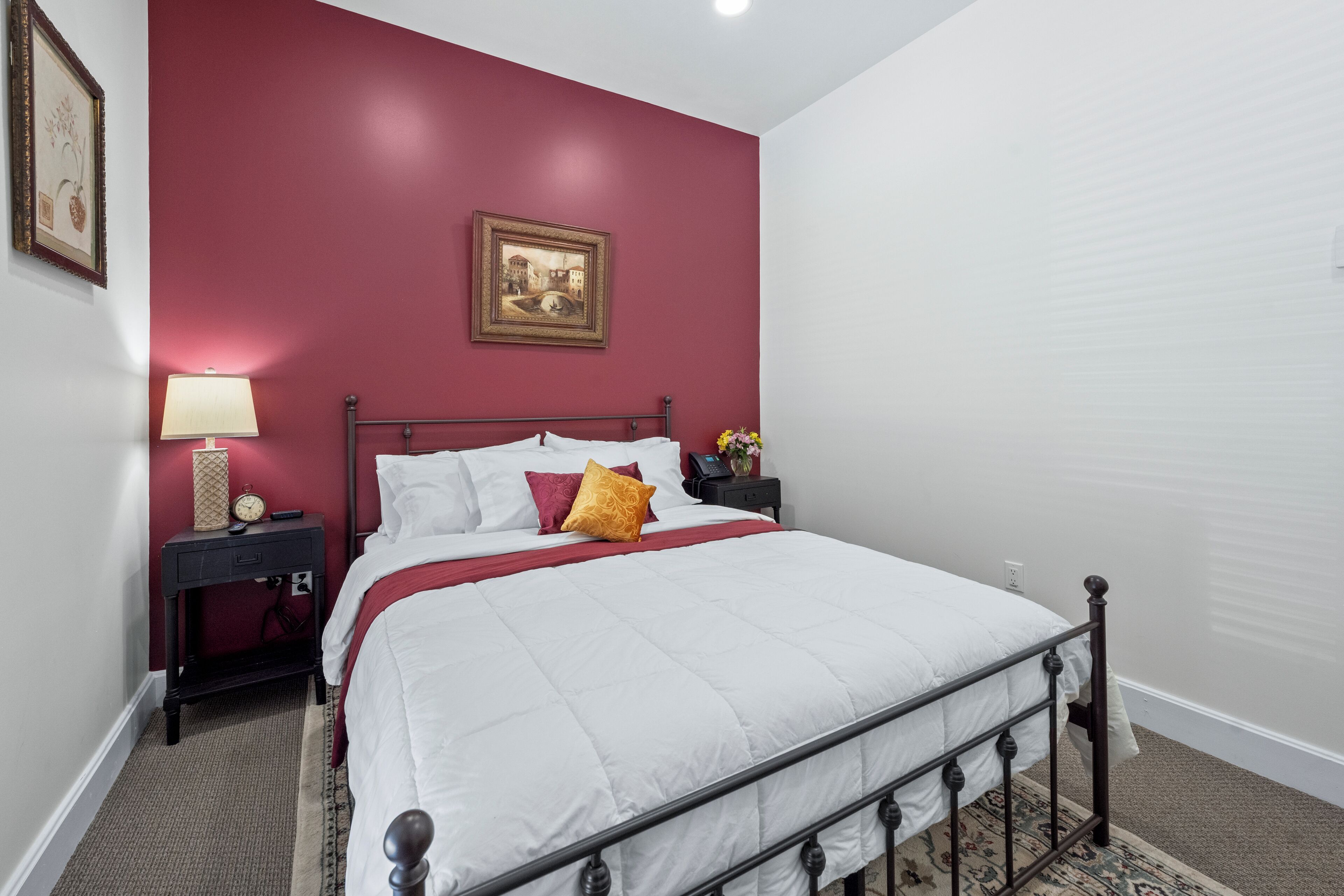 Cama bem arrumada com roupa de cama branca e parede vermelha ao fundo.