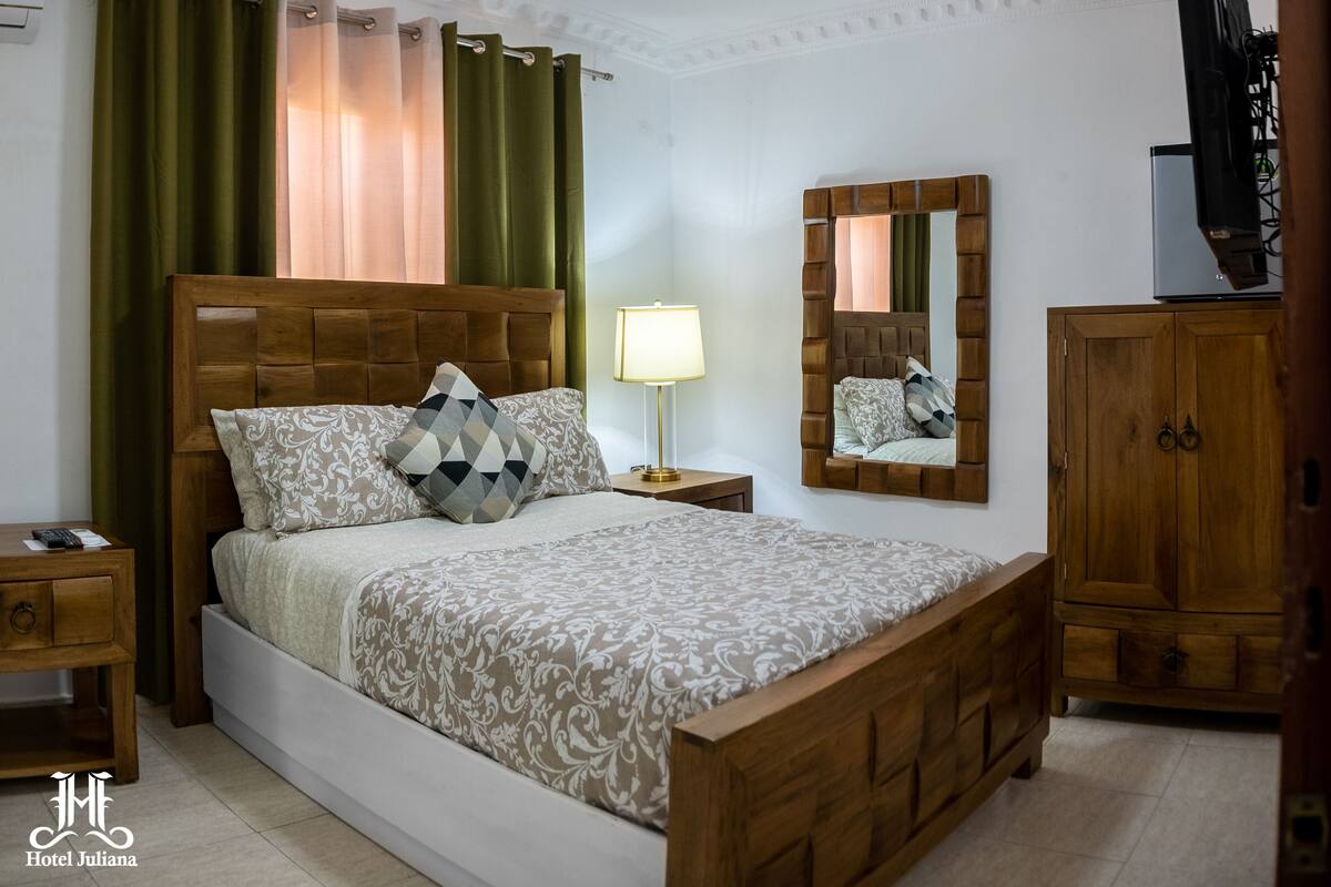 Quarto com cama de madeira, mesa de cabeceira, abajur, espelho e guarda-roupa.