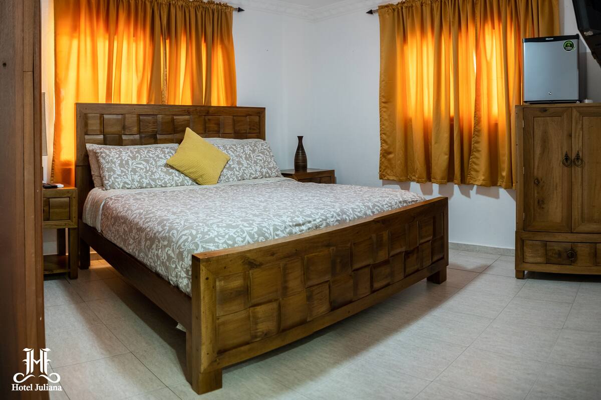 Uma cama de madeira com roupa de cama estampada, uma mesinha de cabeceira e um armário.