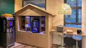 Uma cozinha compacta com bancada de madeira, máquina de café, dispensador de frutas, torradeira e uma janela com vista para a rua.