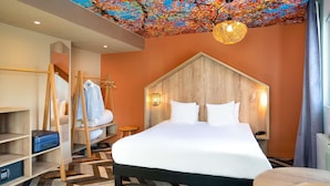 Quarto de hotel com cama grande, guarda-roupa, escrivaninha e um mural no teto.