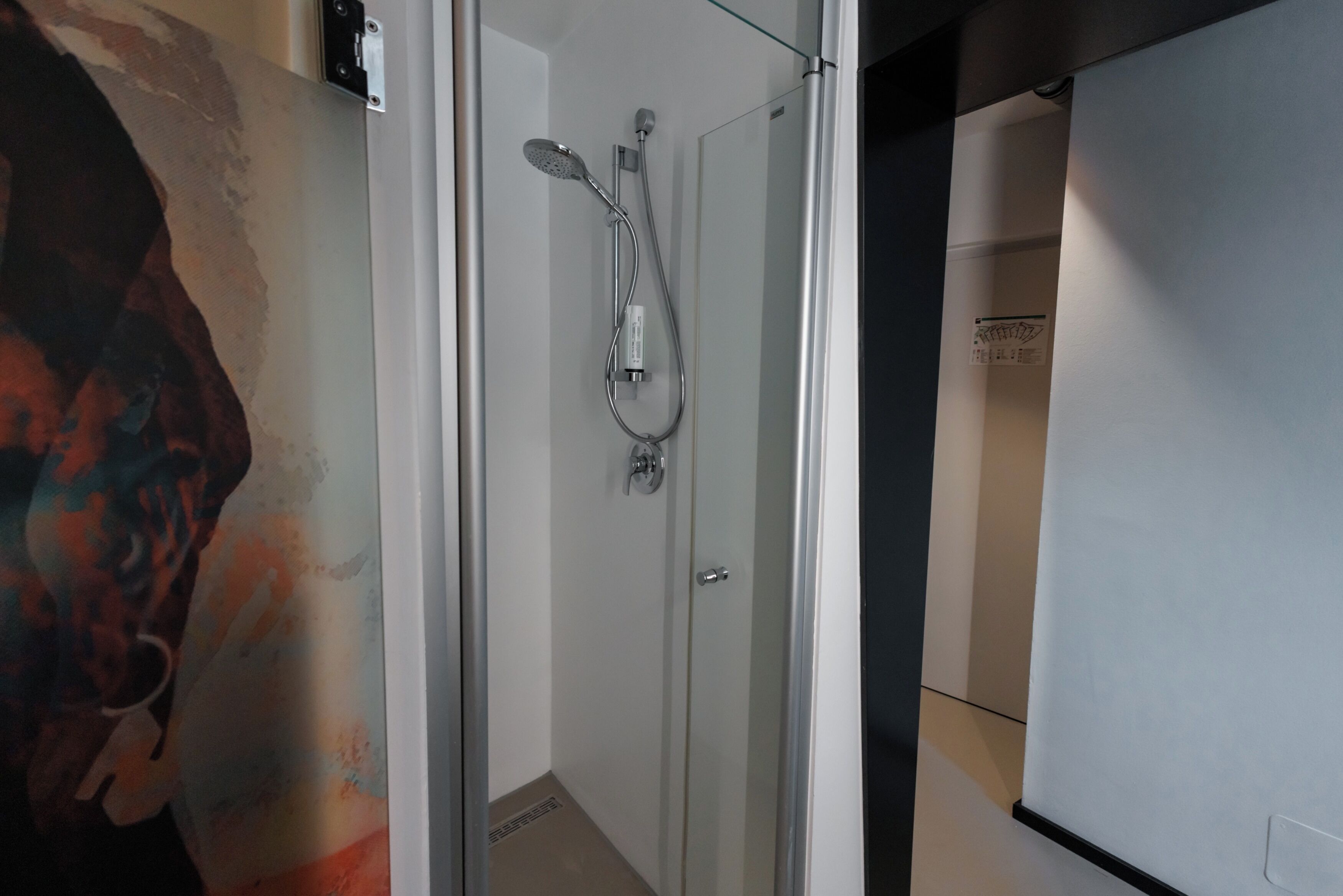Uma casa de banho moderna com cabine de duche em vidro, painel de comando visível e porta com puxador.
