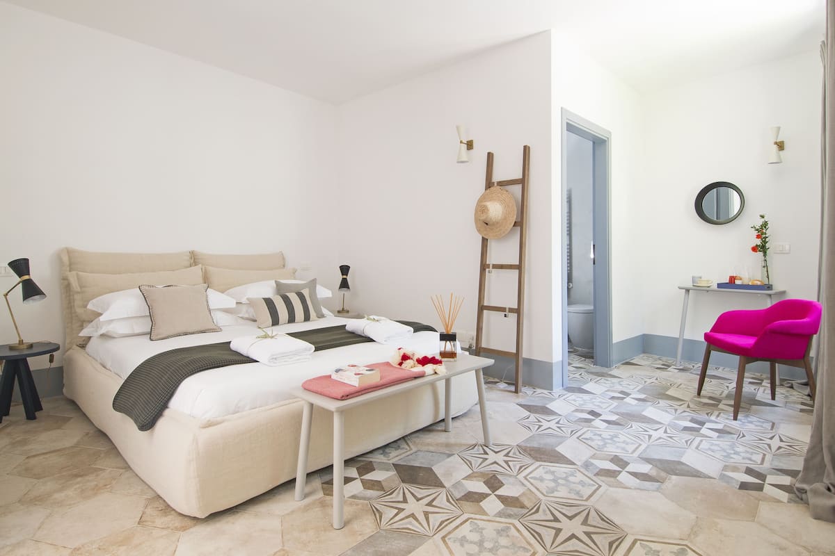 Um quarto com cama, mesa de cabeceira, abajur e uma cadeira.