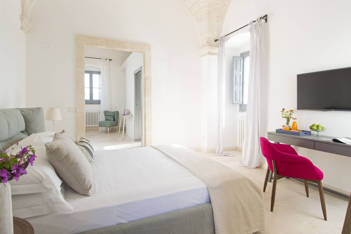 Quarto com cama, escrivaninha, cadeira e televisão.