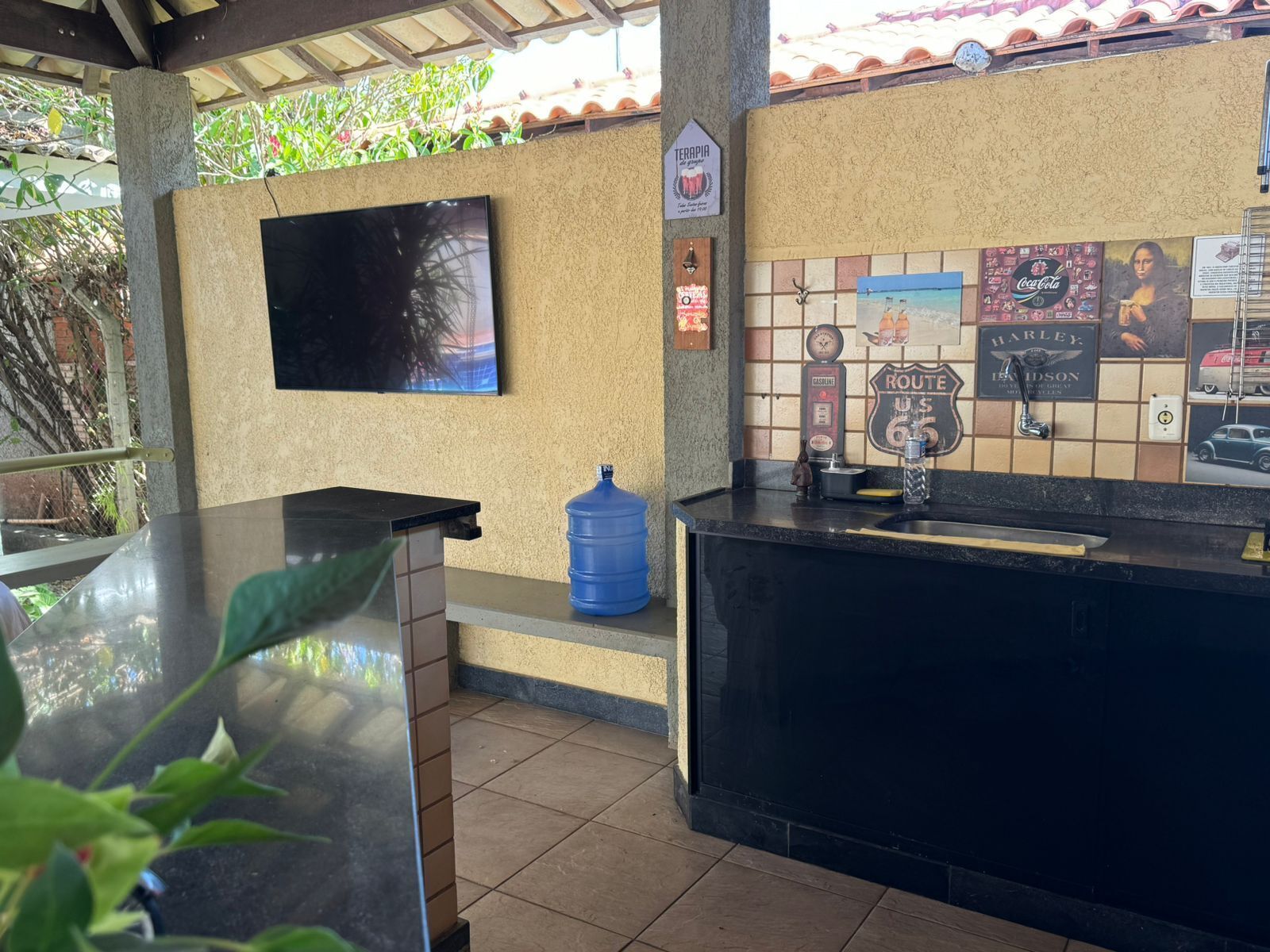 Restaurante com balcão preto, grande dispensador de água azul e parede decorada com placas antigas e uma pintura.