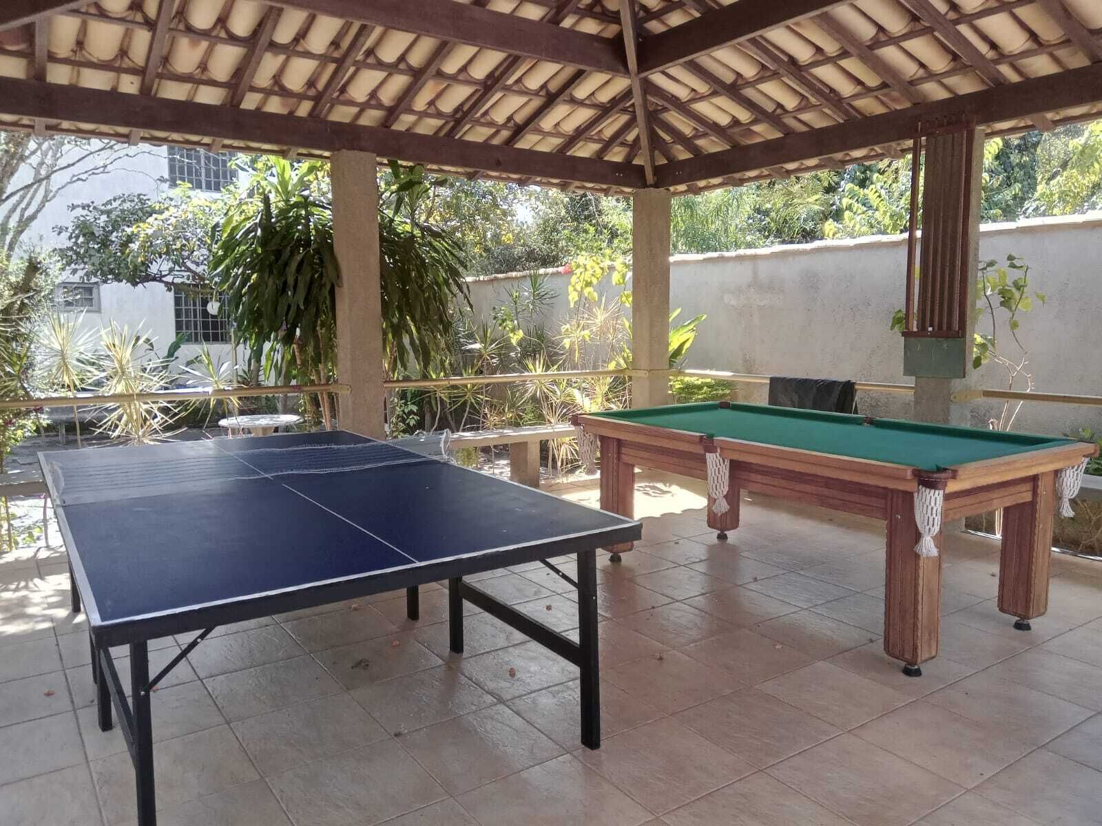 Uma área externa coberta com mesa de pingue-pongue e mesa de bilhar.