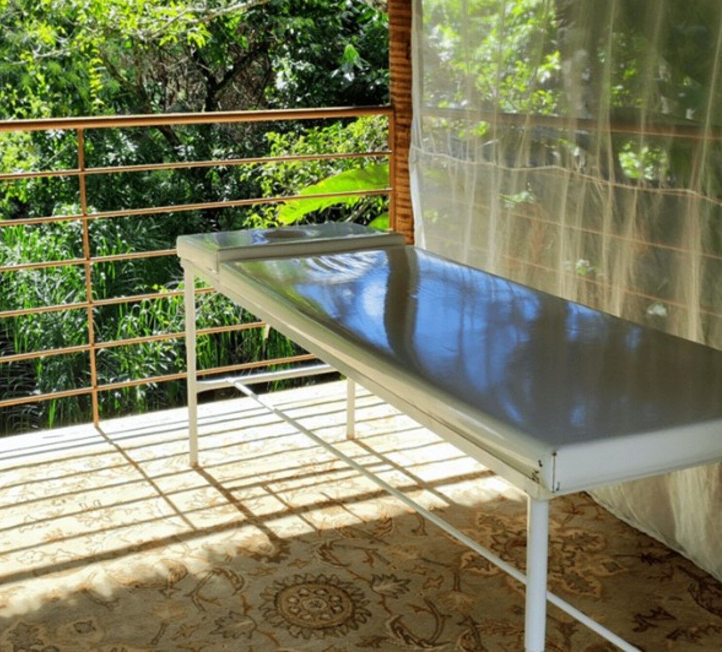 Uma varanda com grade de metal, uma mesa e uma cadeira.