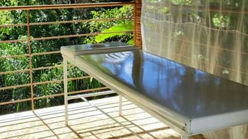 Uma varanda com grade de metal, uma mesa e uma cadeira.