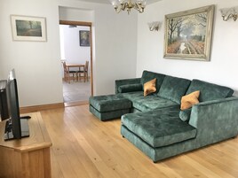 Uma sala de estar com sofá seccional, televisão e um espaço de refeições ao fundo.